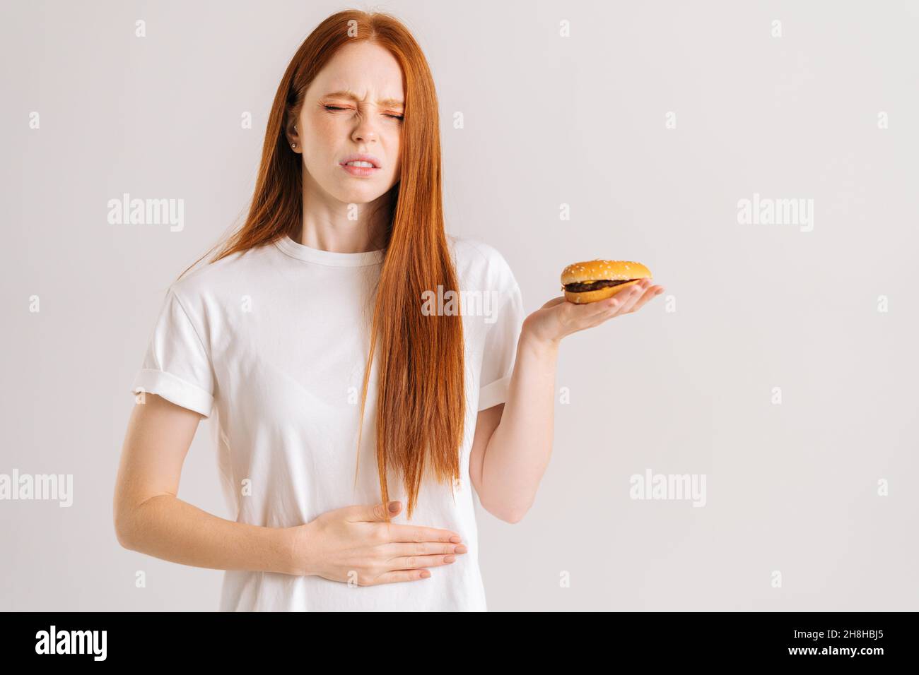 Studio portrait of displeased young woman with disgust holding burger ...
