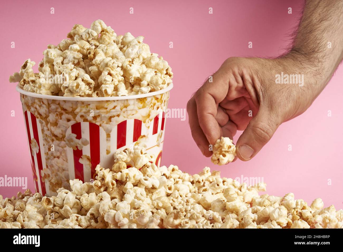 Hand grabbing popcorn out of bucket on pink background Stock Photo - Alamy