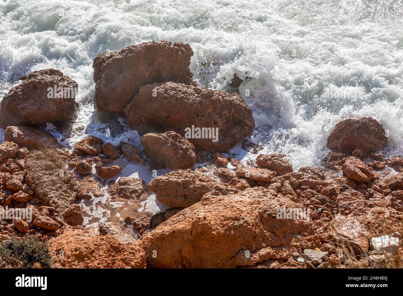 Seafoam. Sea waves with foam crashing on red rocks on the coast of ...