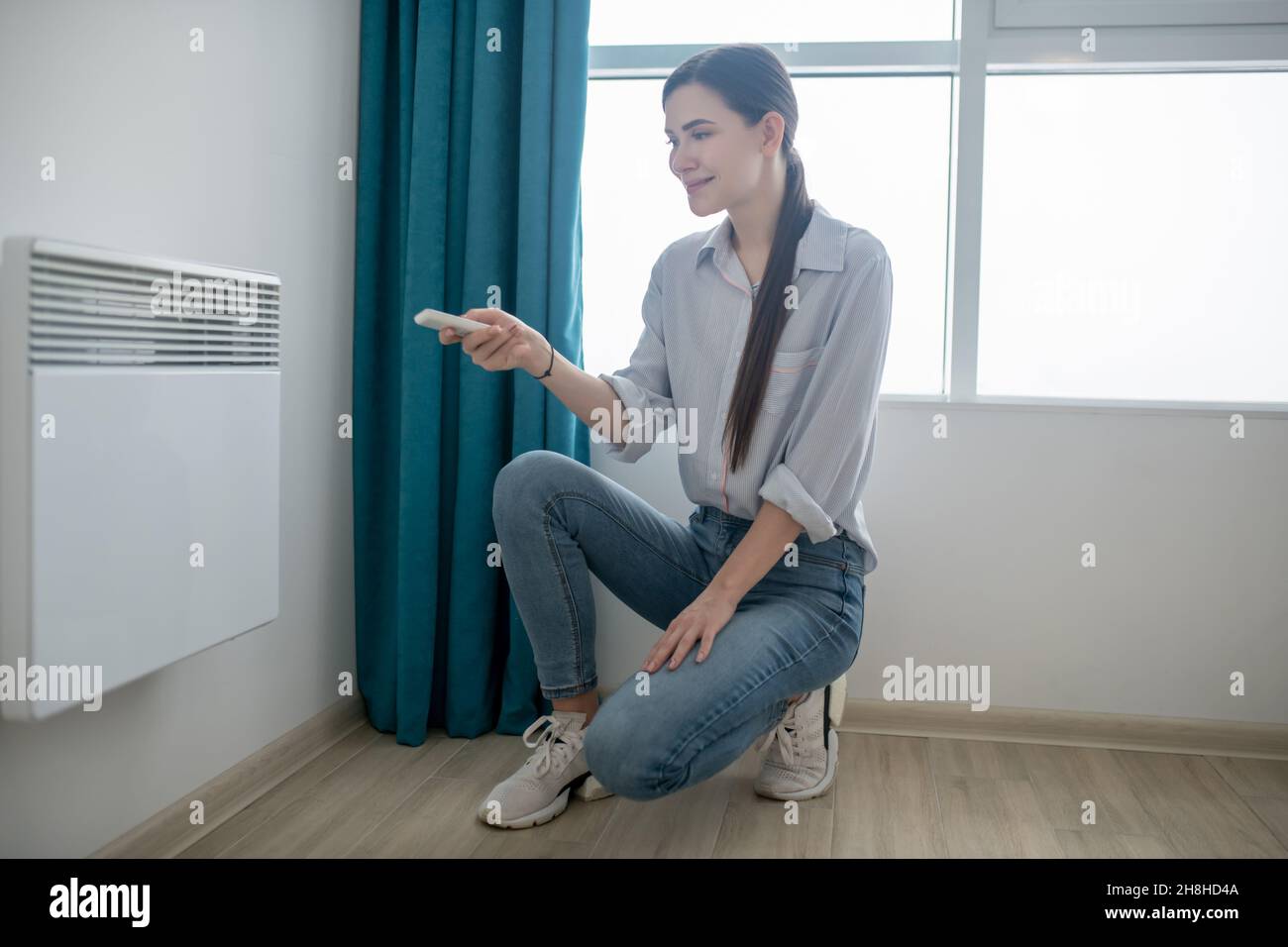 Woman using a remote control for heating a room Stock Photo - Alamy