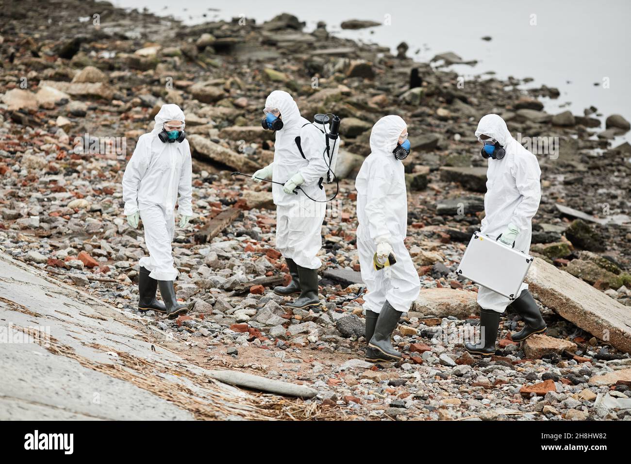 Group of workers wearing hazmat suits walking by water outdoors, toxic ...
