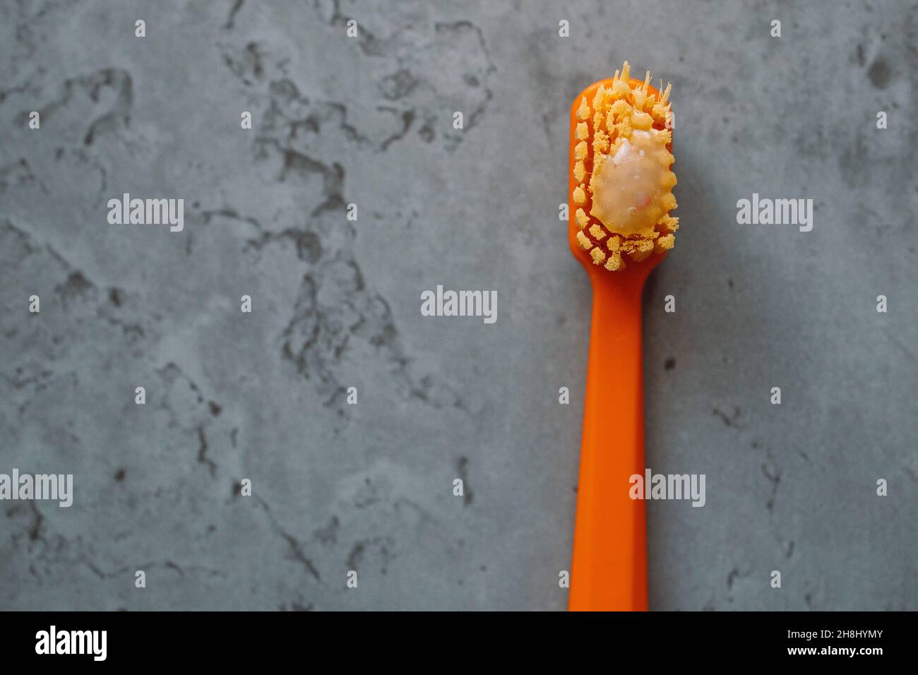 Orange plastic toothbrush with toothpaste on gray concrete table ...