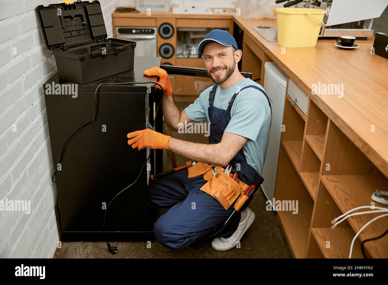 Joyful young man fixing fridge in kitchen Stock Photo - Alamy