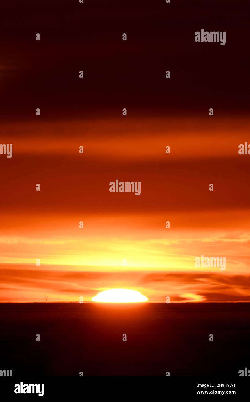 Sun half visible above the sea casting an orange beam of light into the ...