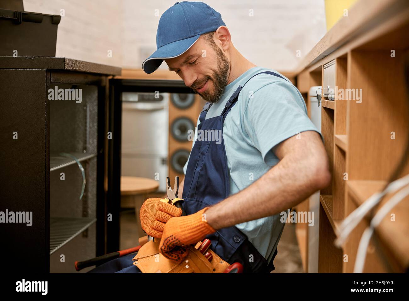 Cheerful repairman choosing tool to fix fridge Stock Photo - Alamy