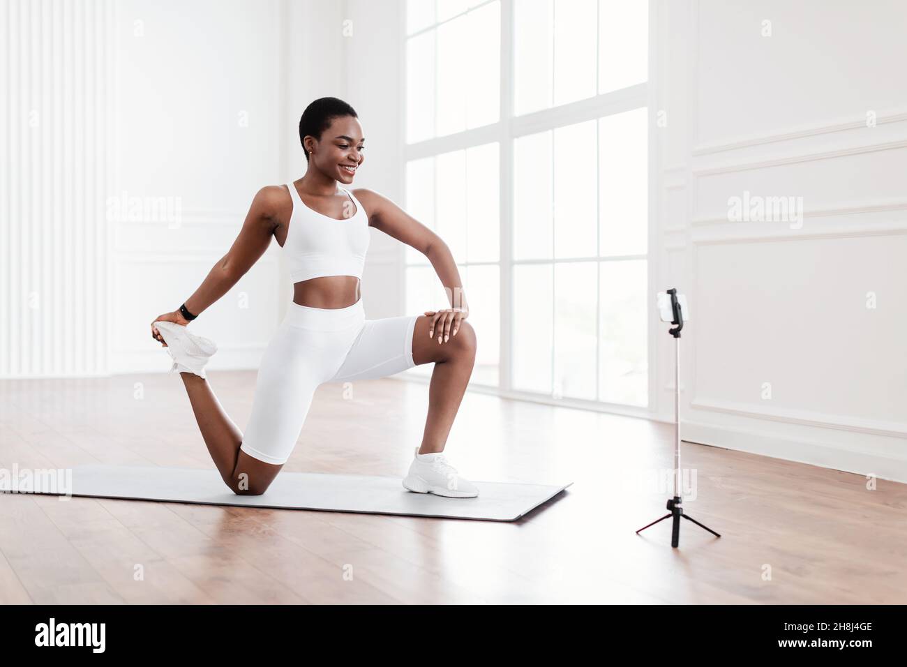 Cheerful black woman stretching leg muscles using cellphone Stock Photo ...