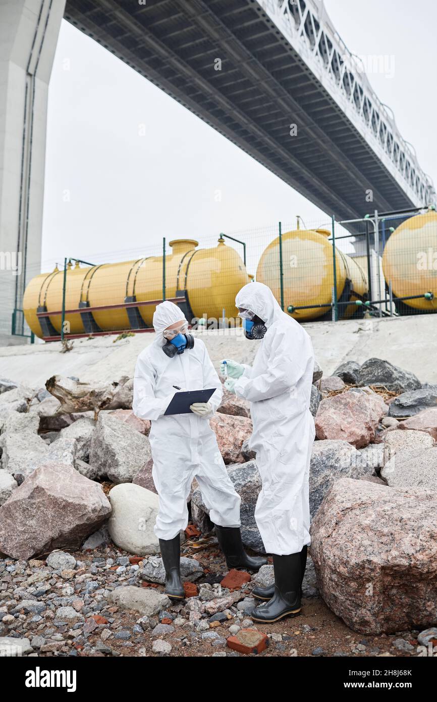 Full length portrait of two scientists wearing hazmat suits collecting ...