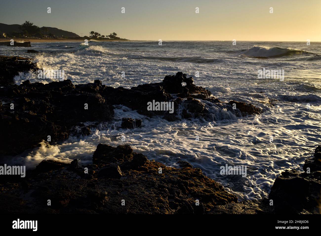 Sunrise as the surf crashes on and swirls around volcanic lava rocks at ...