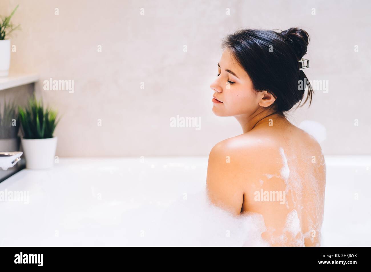 Young Woman Lies In White Bath Of Foam With Her Eyes Closed Spa