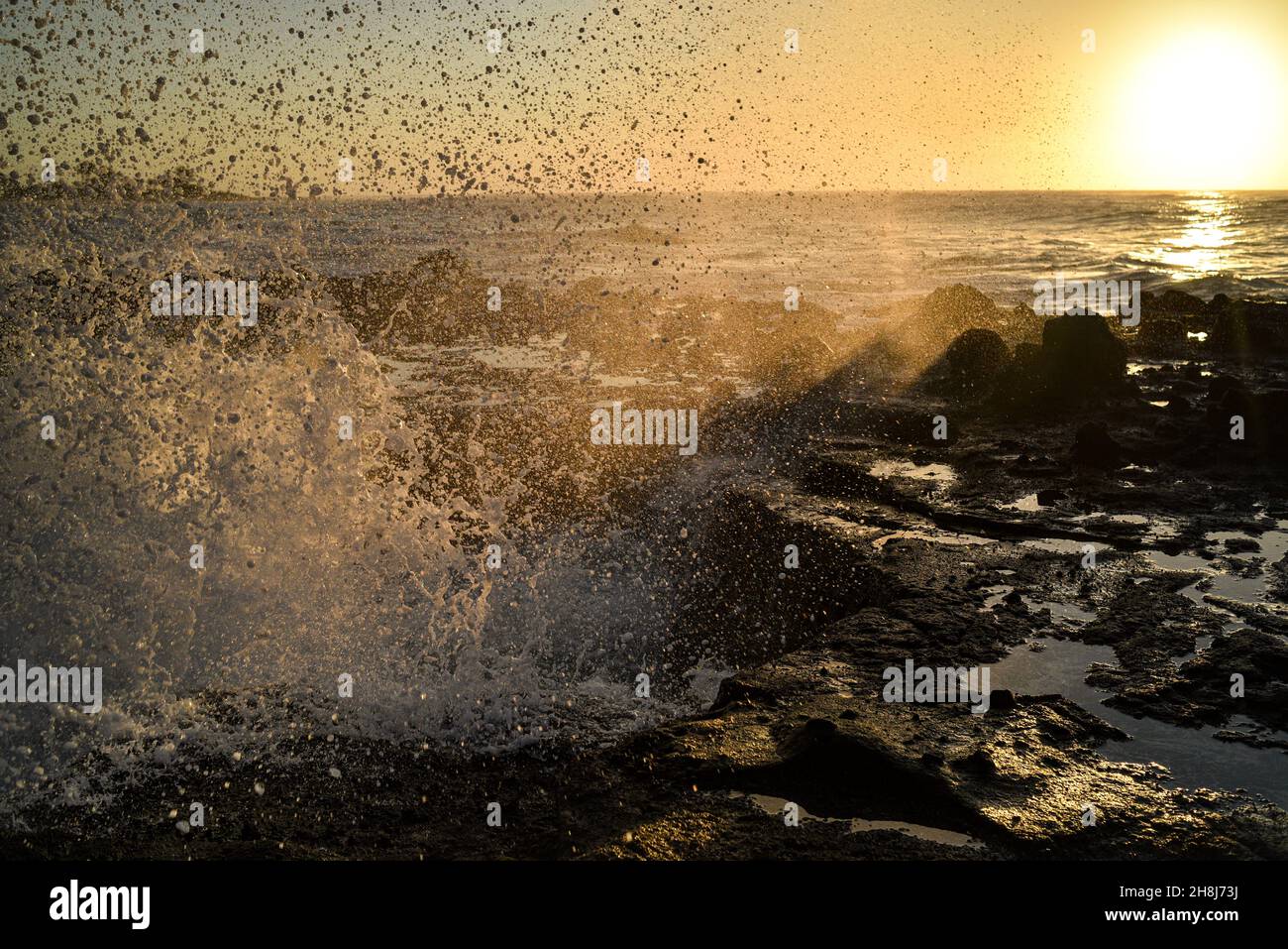 Sunrise as the surf crashes on and swirls around volcanic lava rocks ...