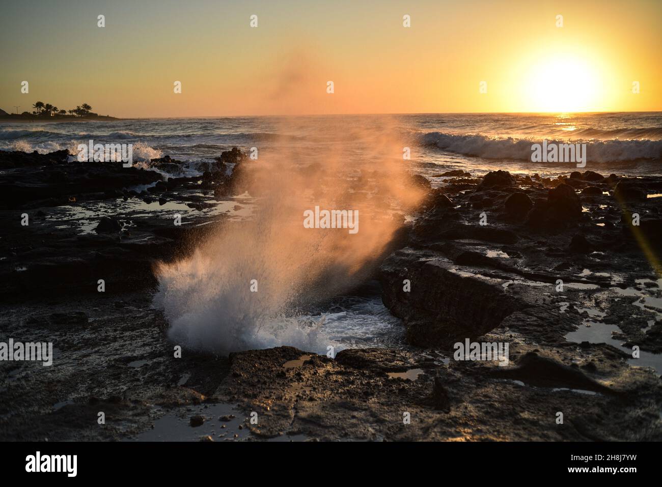 Sunrise as the surf crashes on and swirls around volcanic lava rocks ...
