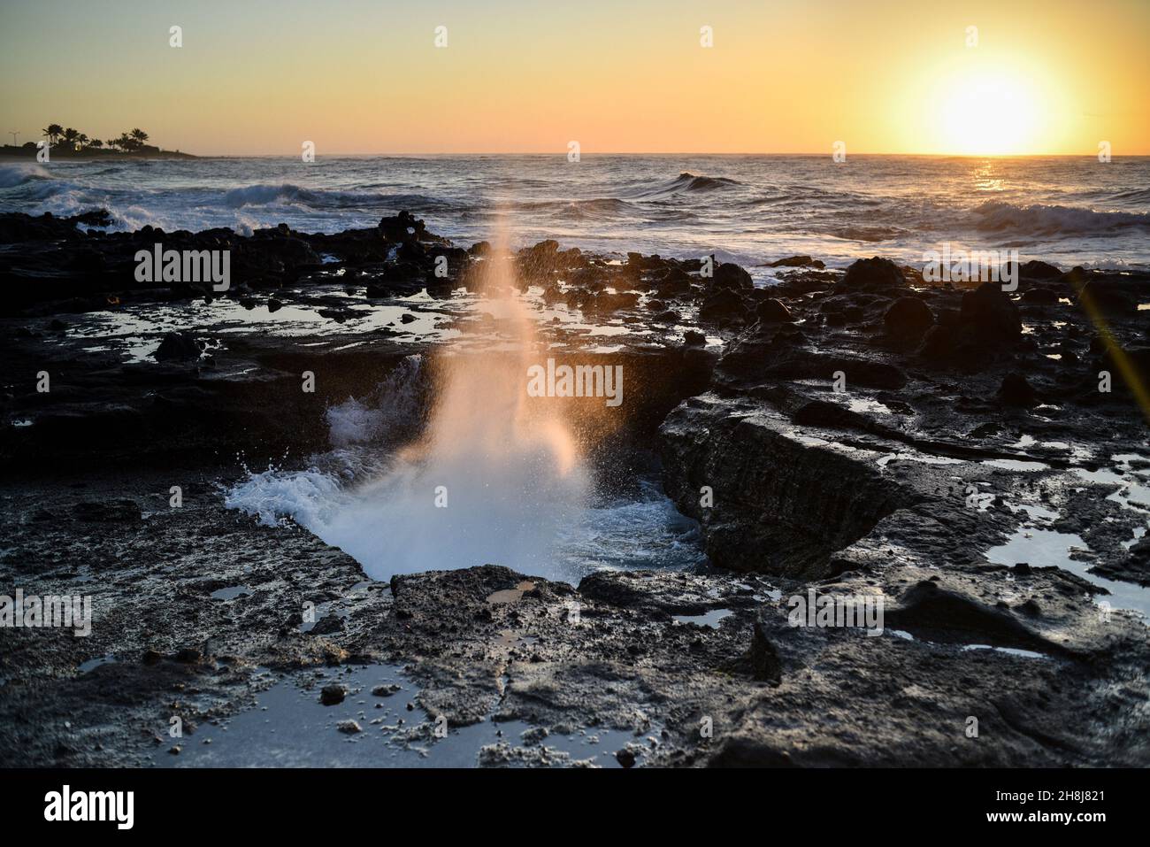 Sunrise as the surf crashes on and swirls around volcanic lava rocks ...