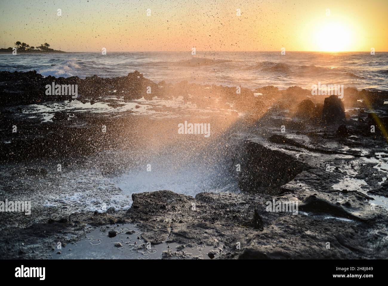 Sunrise as the surf crashes on and swirls around volcanic lava rocks ...