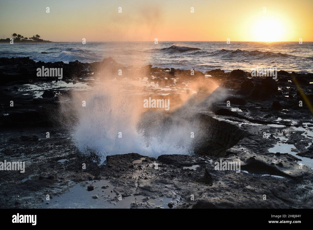 Sunrise as the surf crashes on and swirls around volcanic lava rocks ...