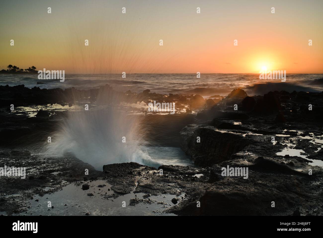 Sunrise as the surf crashes on and swirls around volcanic lava rocks ...