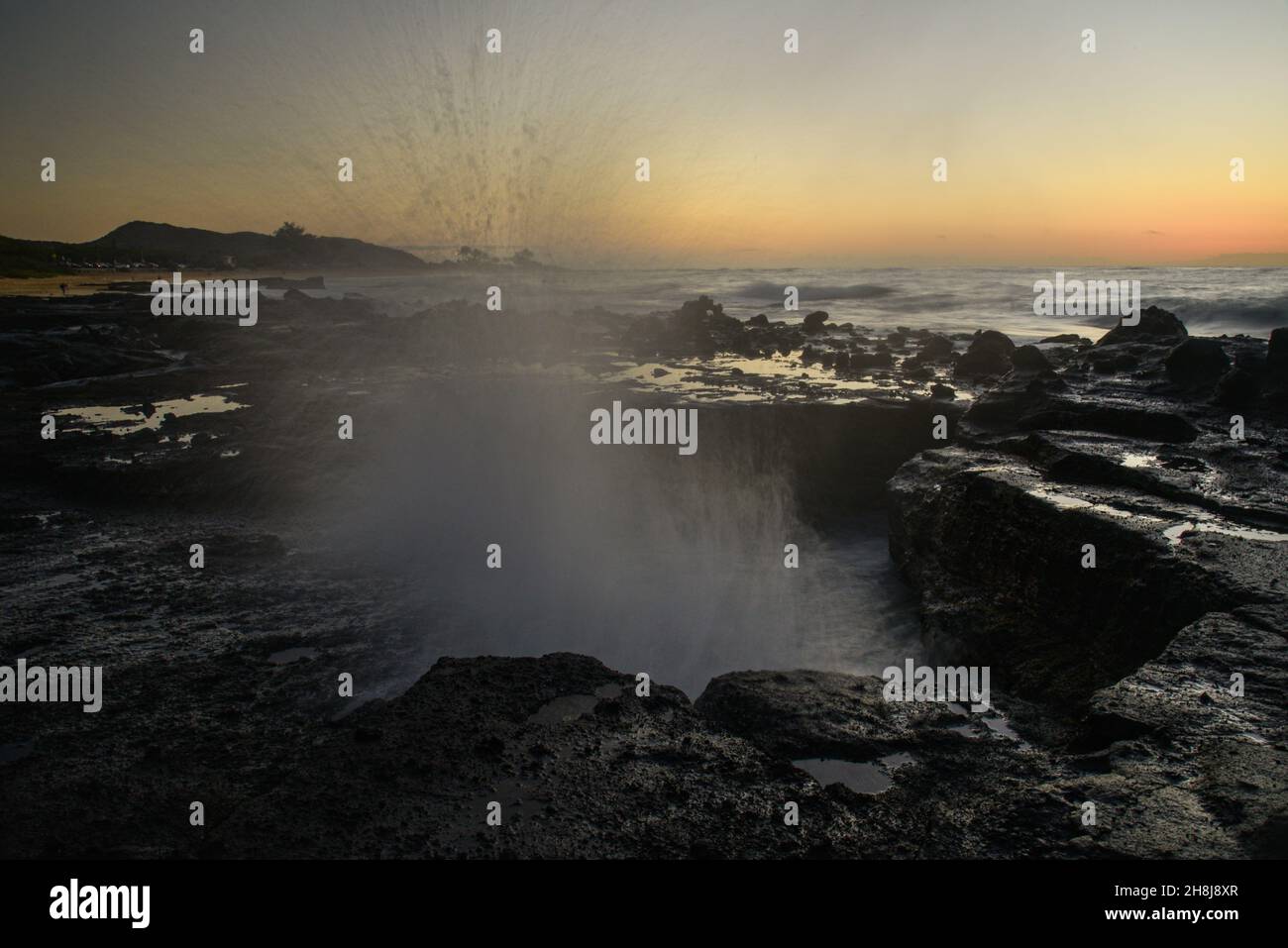 Sunrise as the surf crashes on and swirls around volcanic lava rocks ...