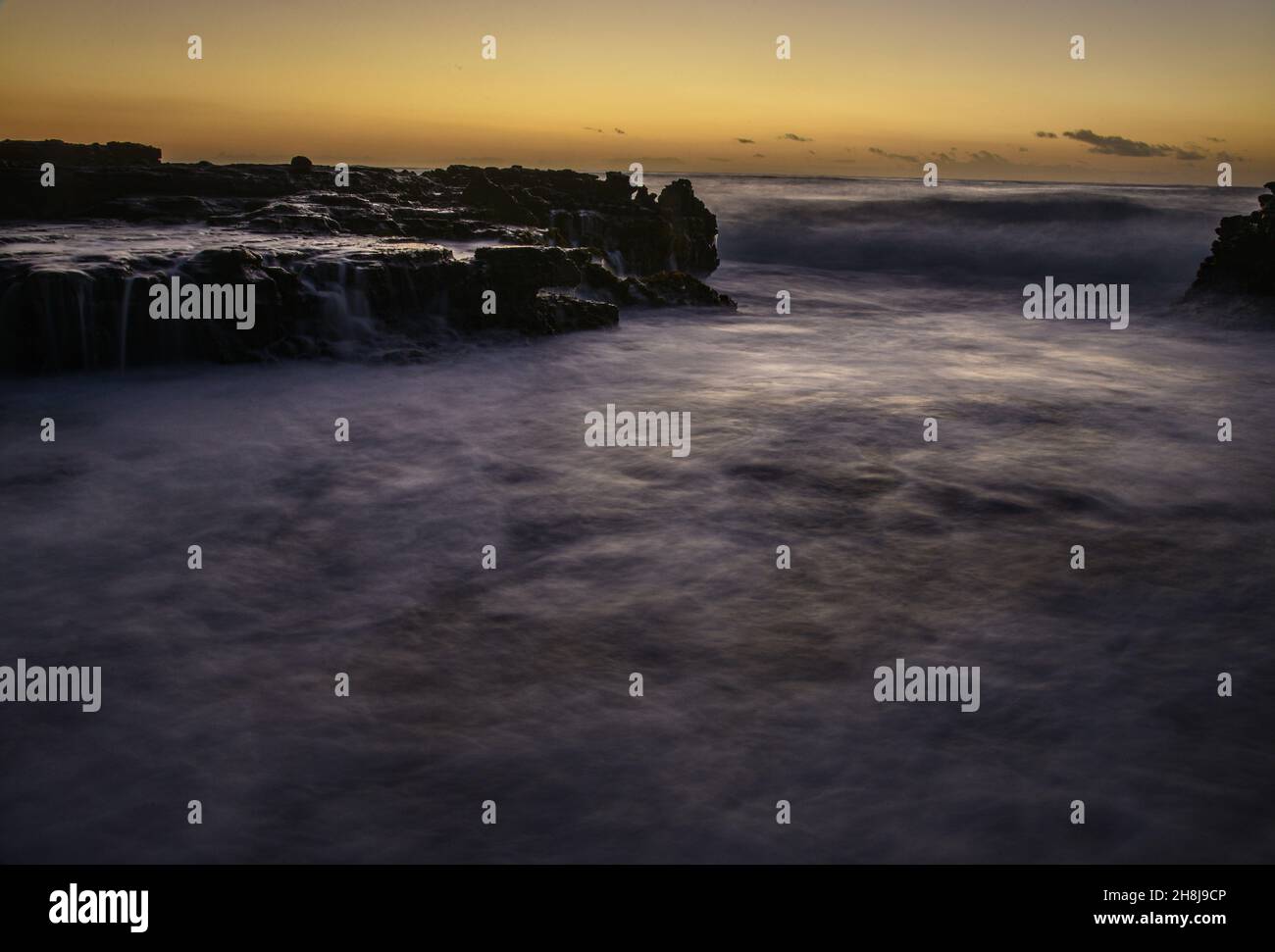 Sunrise as the surf crashes on and swirls around volcanic lava rocks at ...