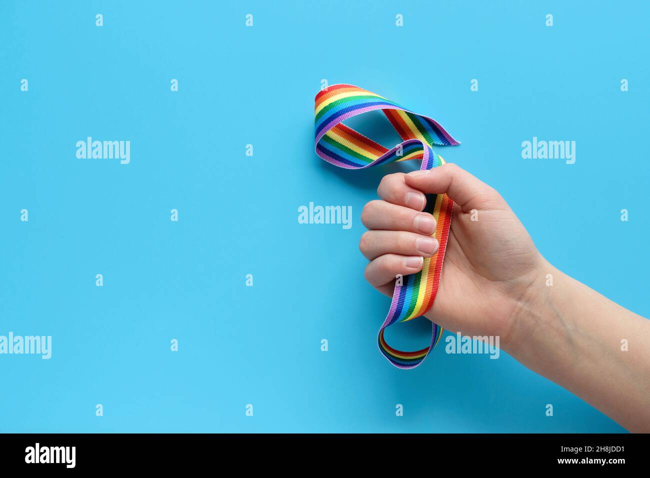 Rainbow ribbon in child hand. Blue mint paper background Stock Photo ...