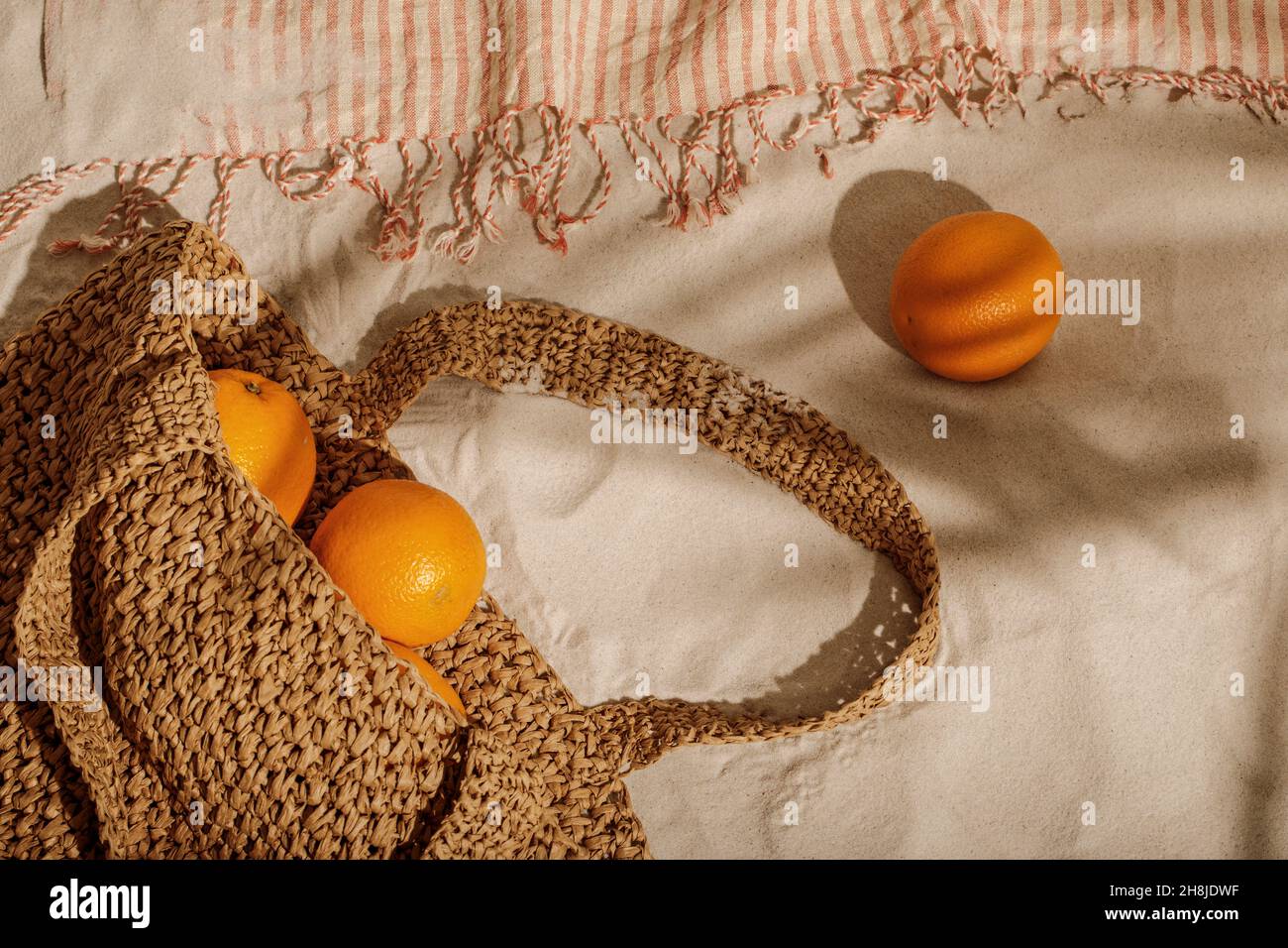 Fresh oranges falling out from woven bag on sandy beach. Linen beach ...