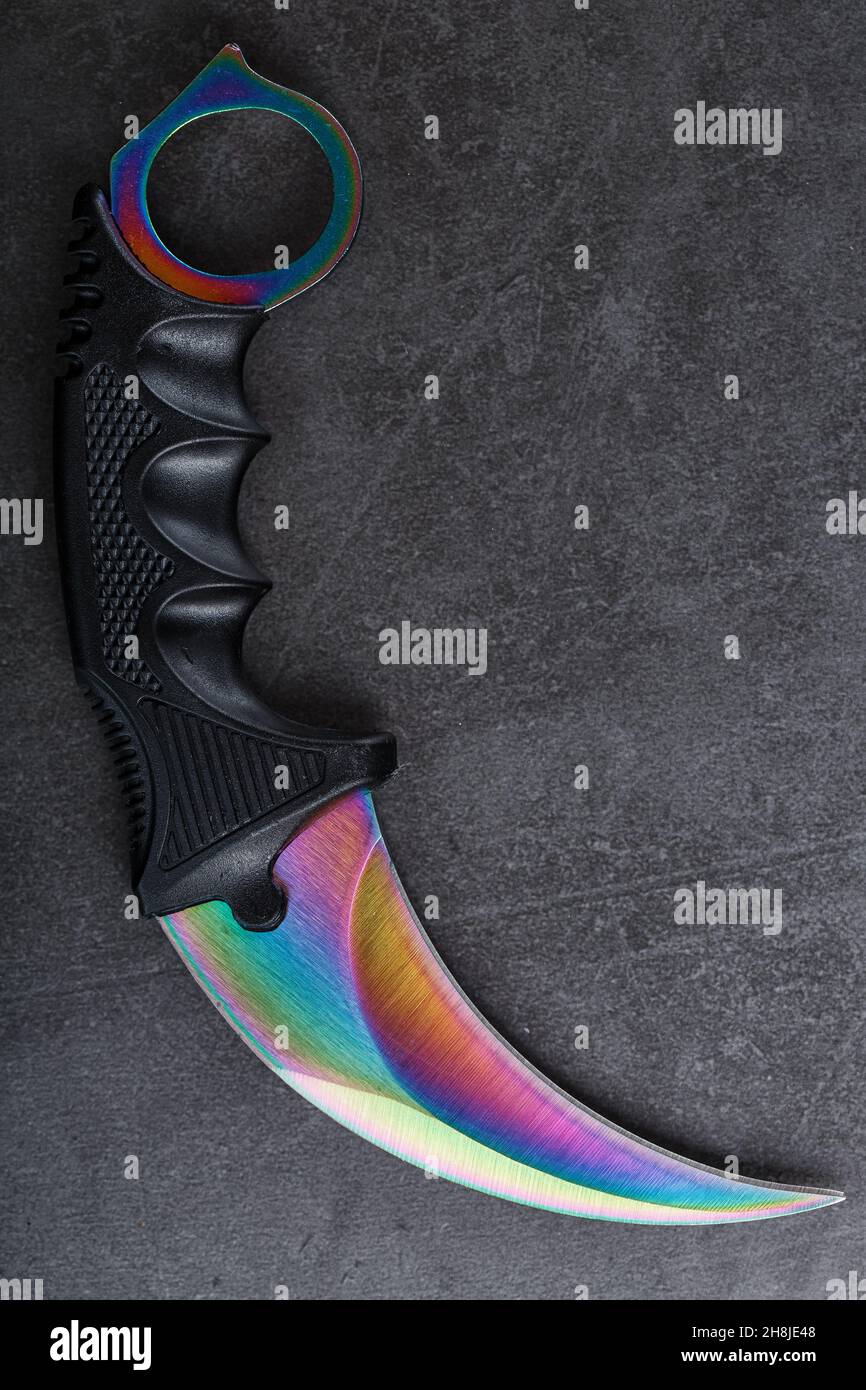 Kerambit dagger with a rainbow-colored blade on a dark textured ...