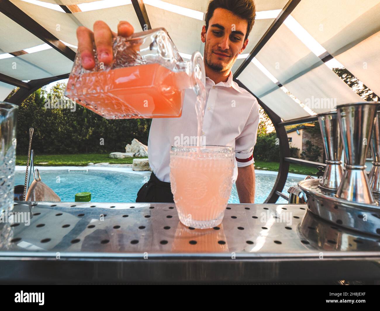 Young bartender making a cocktail at the outdoor bar on the background ...