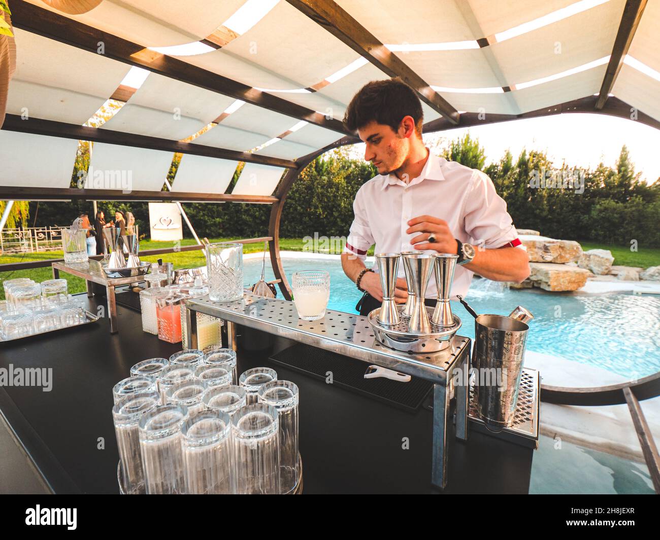 Young bartender making a cocktail at the outdoor bar on the background ...