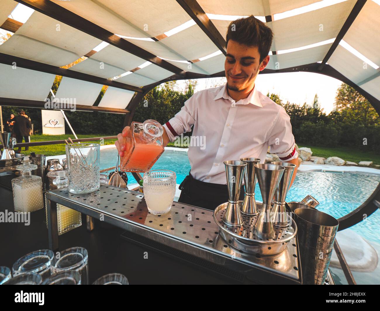 Young bartender making a cocktail at the outdoor bar on the background ...