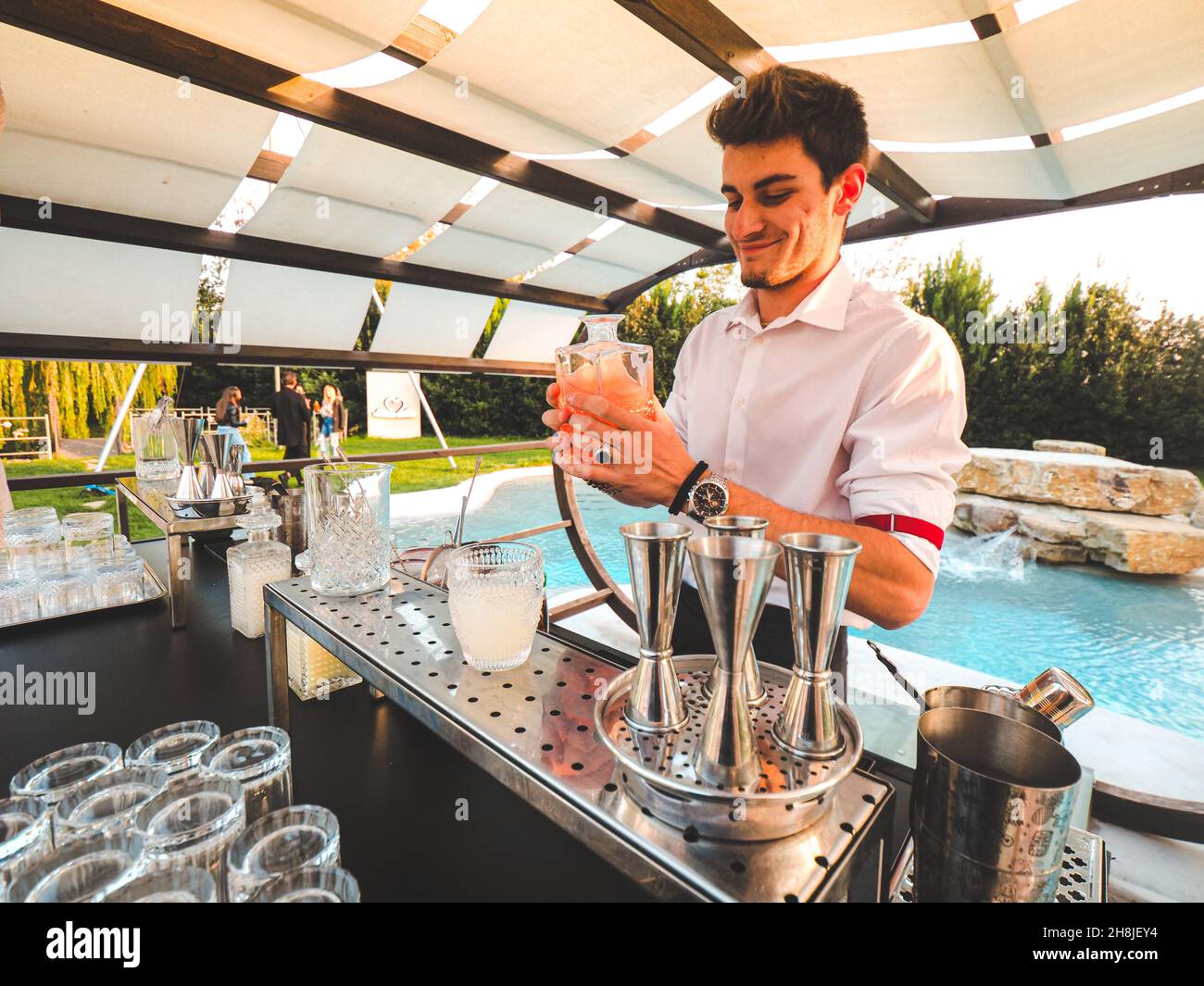 Young bartender making a cocktail at the outdoor bar on the background ...