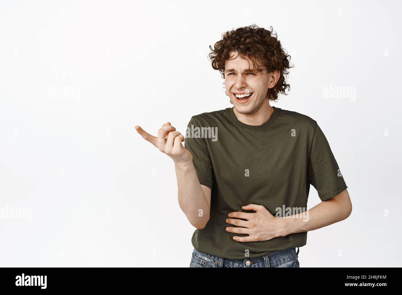Funny young man laughing, pointing at smth hilarious, chuckle and smile ...