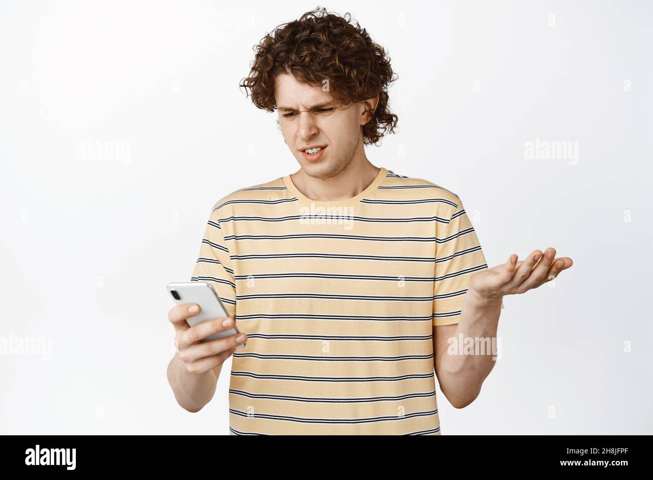 Image of curly guy staring confused at mobile phone, standing in t ...