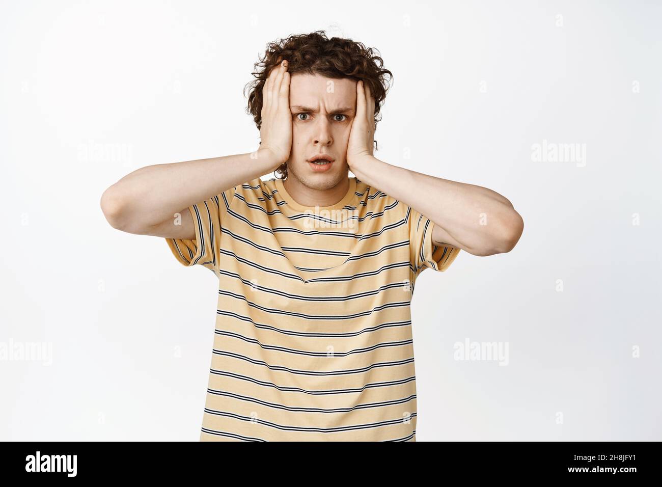 Shocked young man panicking, holding hands on head and staring ...