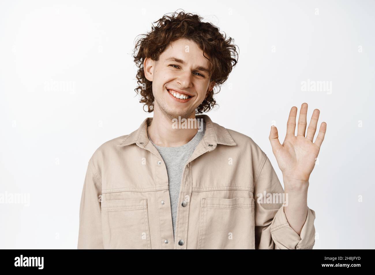 Close up of friendly smiling young man, waves his hand and smiles to ...