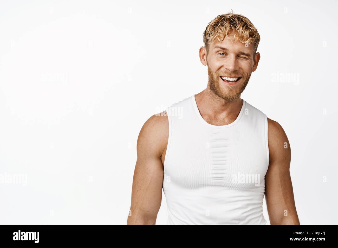 Portrait of sportsman winking and smiling, standing in workout clothes ...