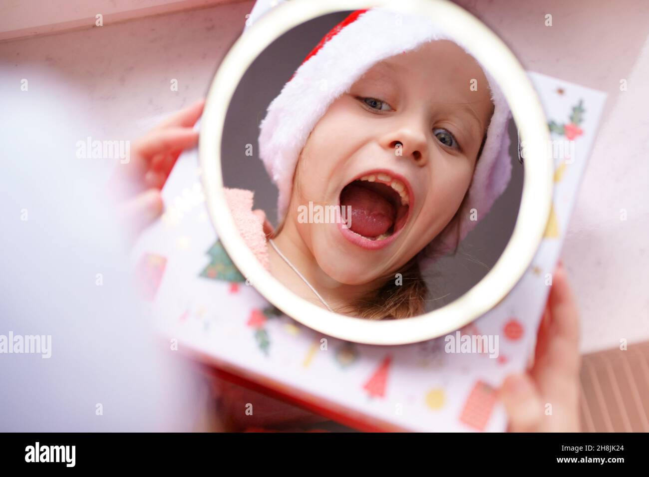 Reflection in the mirror of a Christmas Caucasian girl in Santa's cap ...