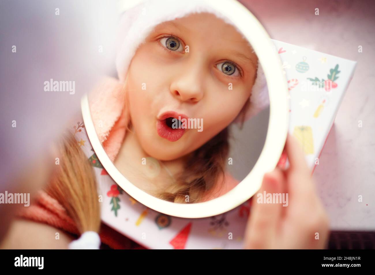 Reflection in the mirror of a Christmas Caucasian girl in Santa's cap ...