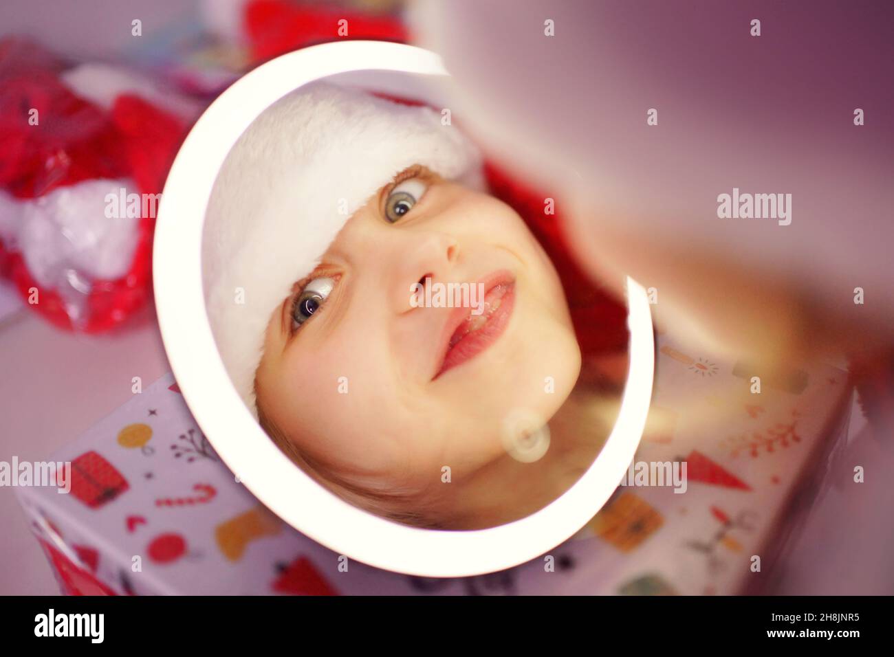 Reflection in the mirror of a Christmas Caucasian girl in Santa's cap ...