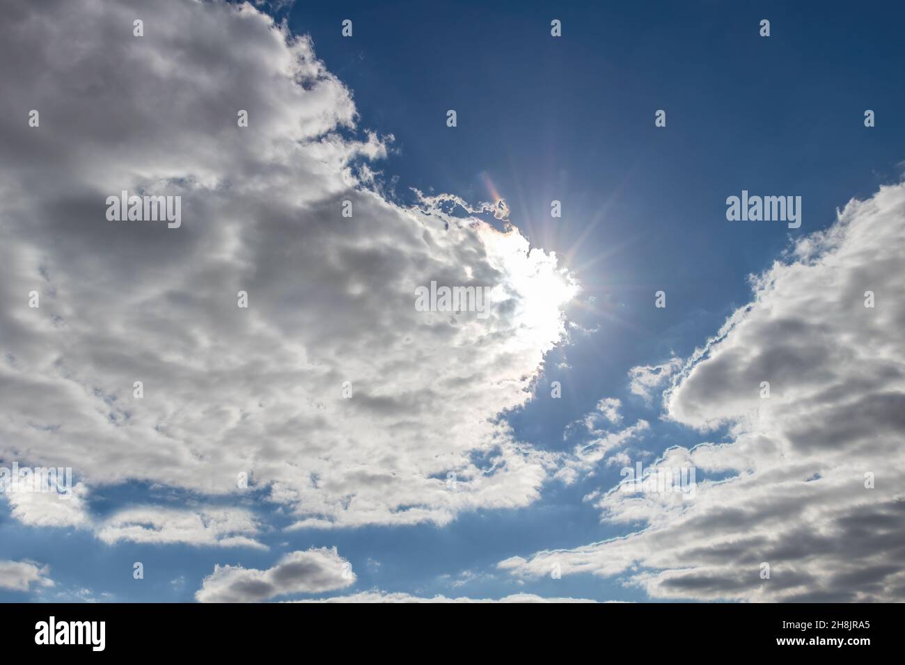 View of a cloudy sky with the sun peeking through the clouds for background Stock Photo - Alamy