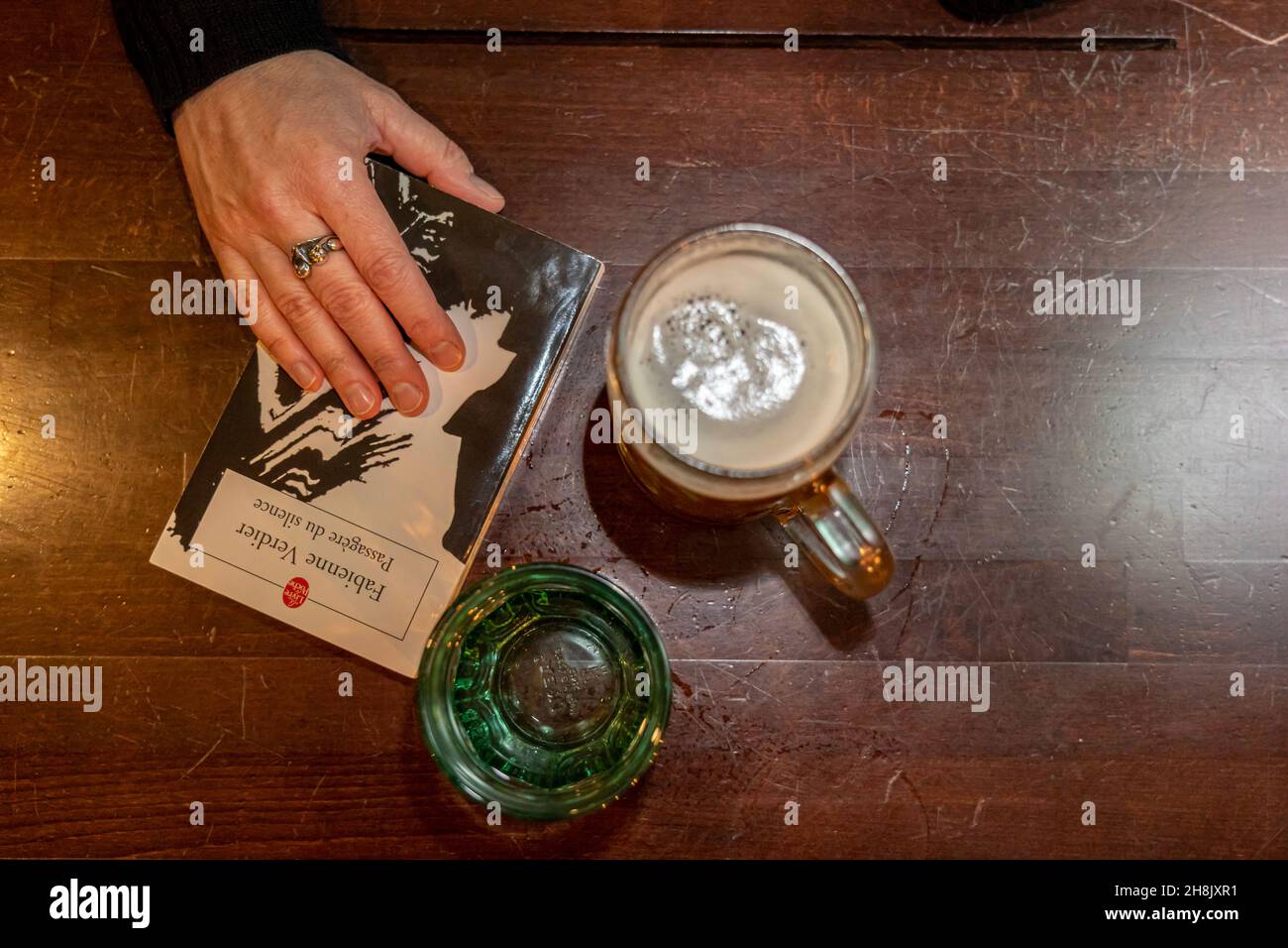 Paris, France - 11 27 2021: A woman reading a book and drinking a beer ...