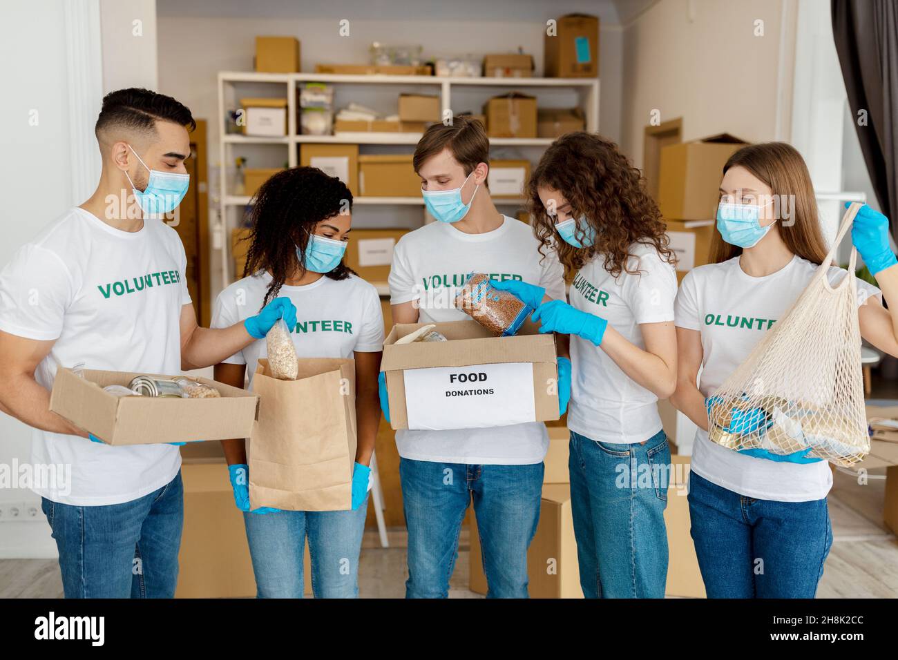 Charity center. Group of diverse young people in medical masks packing ...