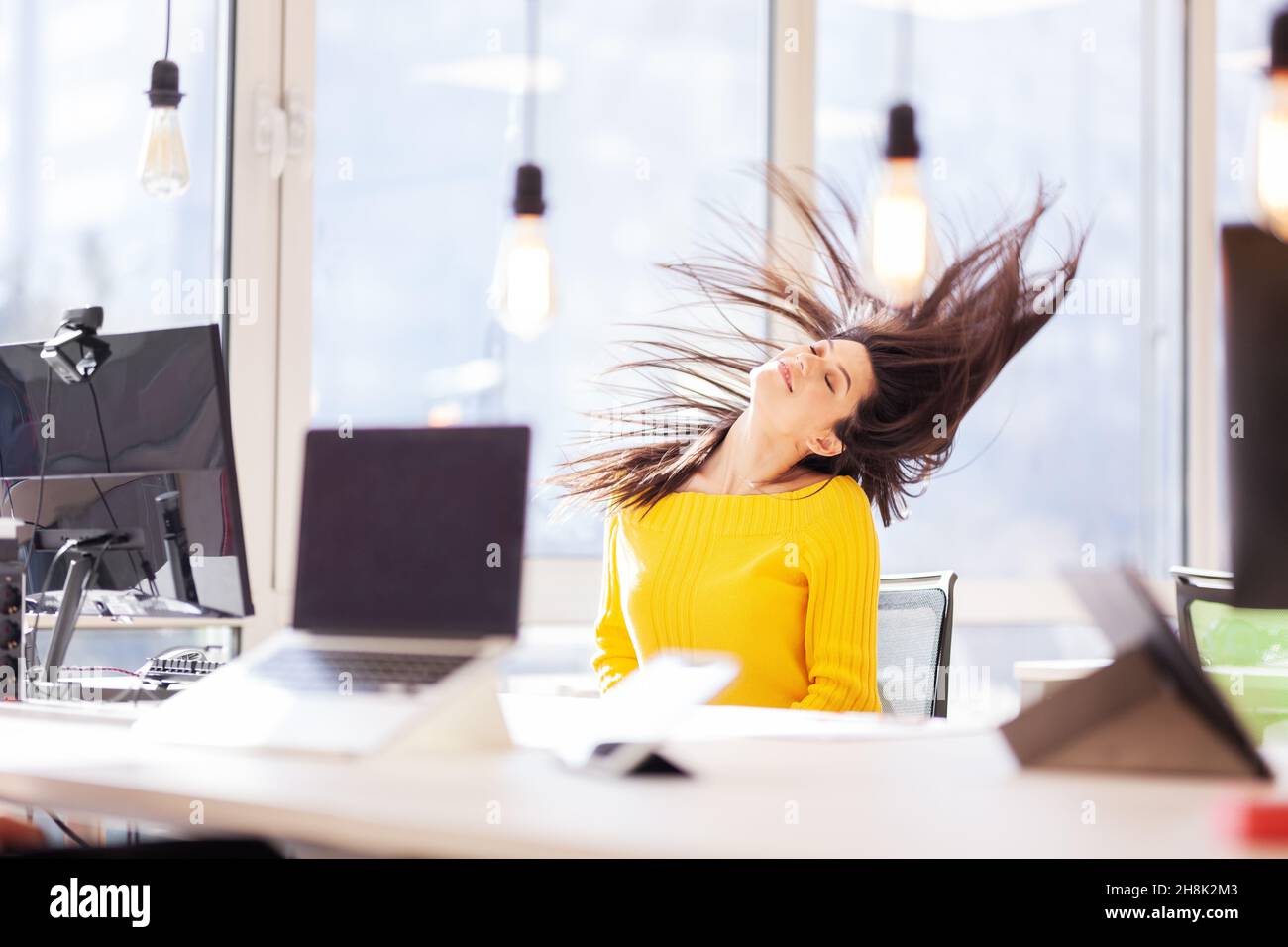 Beautiful girl with long dark hair dancing in modern office. Computer ...
