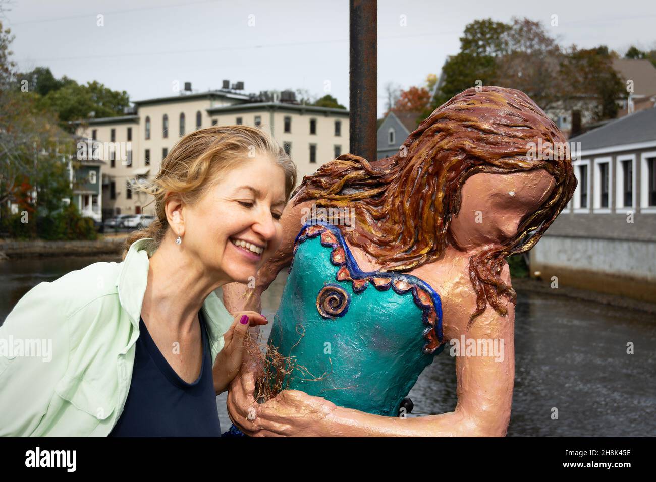 Woman mimics the pose of a mermaid statue looking into the river in ...