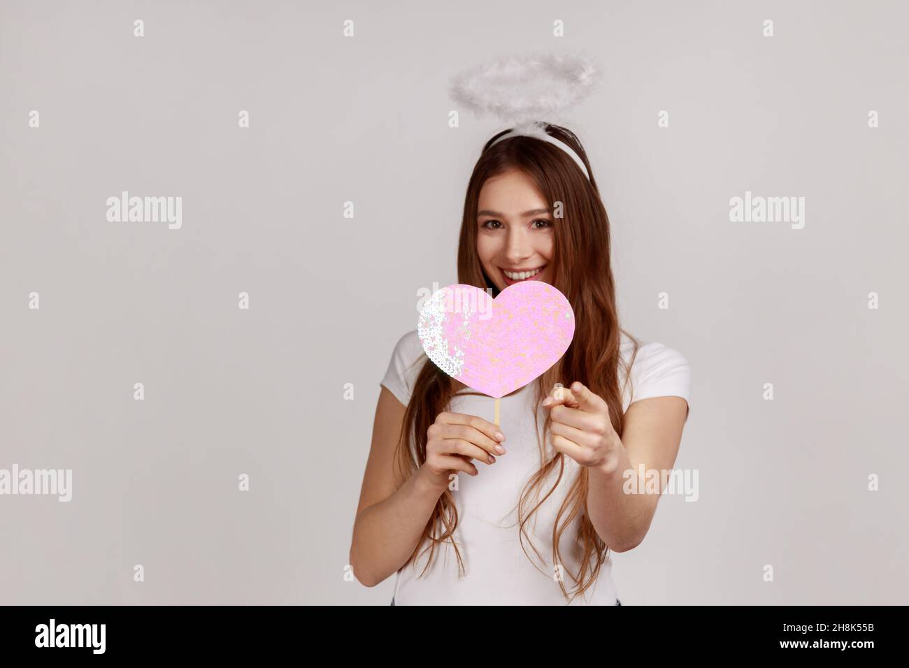 Angelic woman with holy nimbus holding pink paper heart on stick and ...