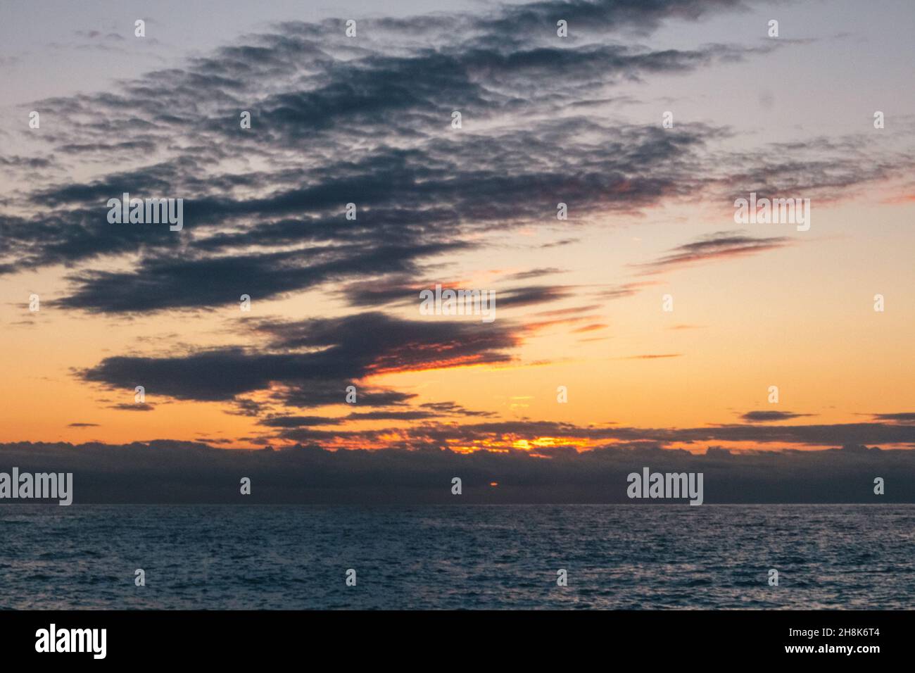 Sunset sky with dark purple clouds above blue rippled sea water ...
