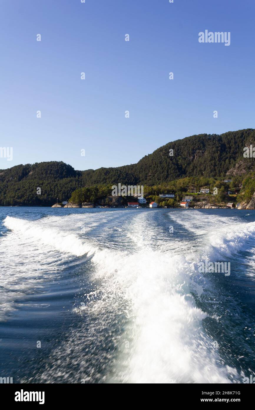 Trail on water surface of fast moving boat with norwegian green forest ...