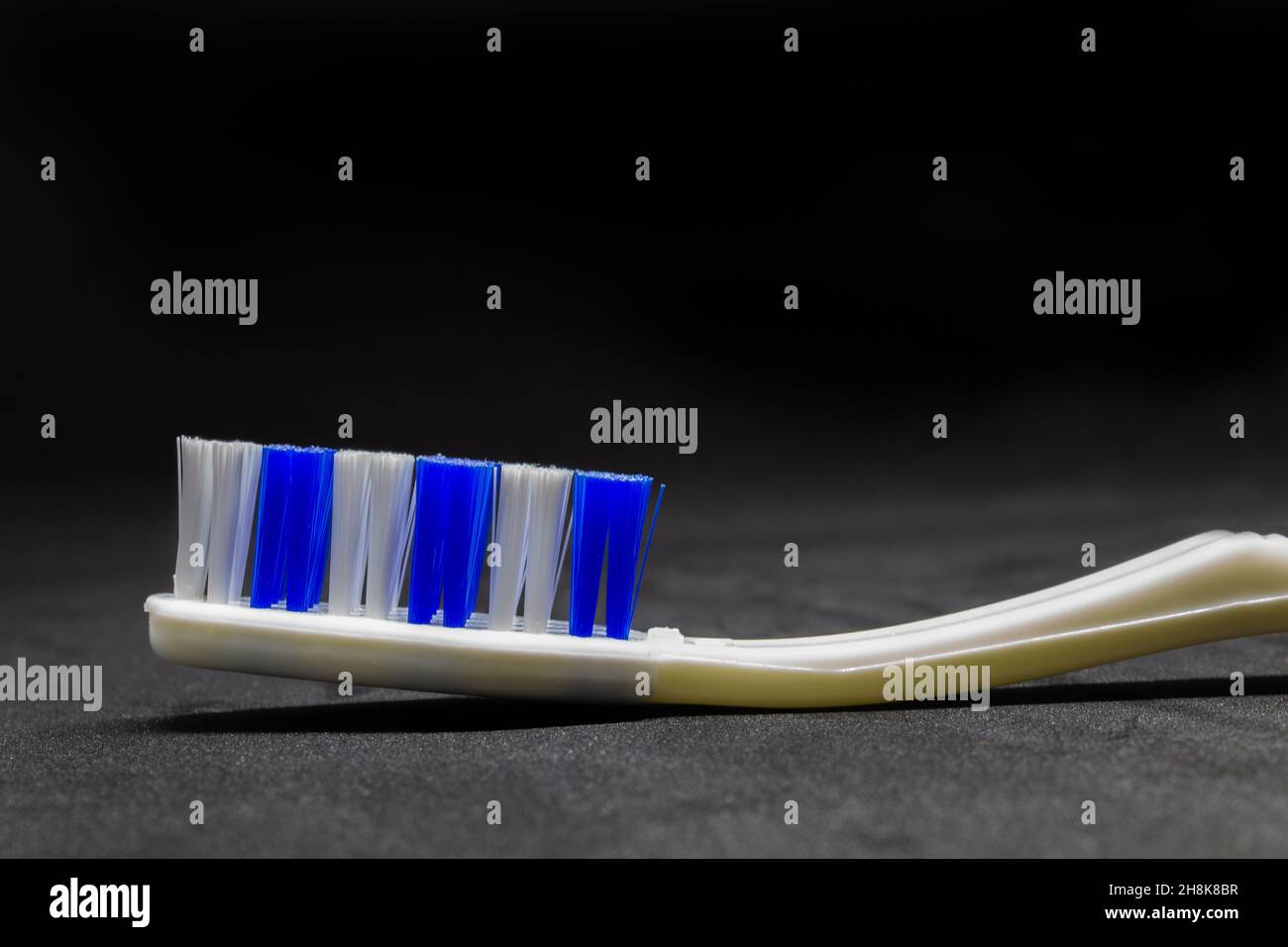 White toothbrush with blue and white bristles in a dark background ...