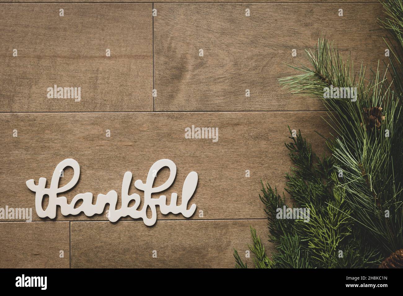 Word thankful on a light wood background with border of evergreen ...
