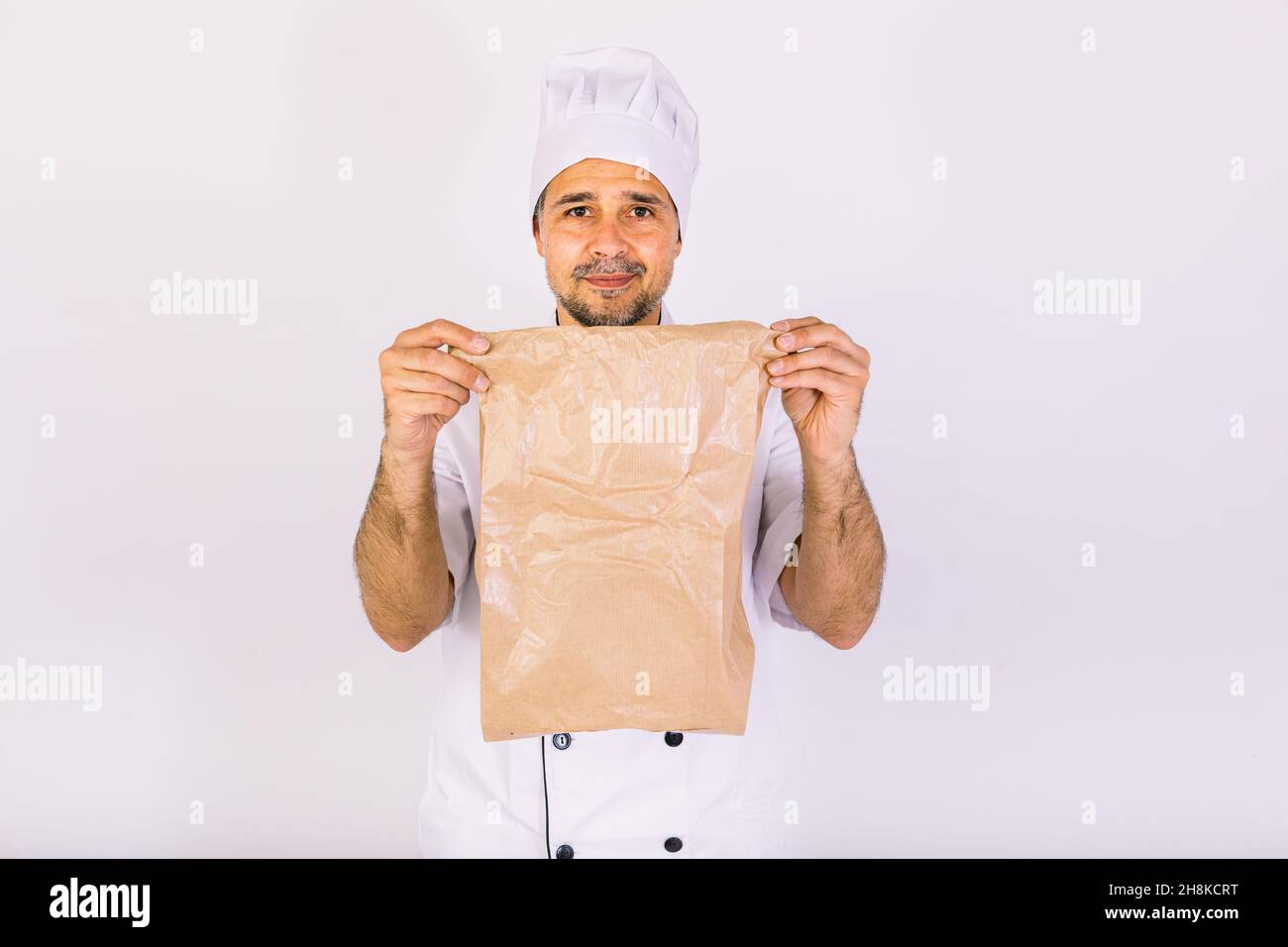 Chef cook wearing white kitchen cap and jacket, holding a paper bag ...