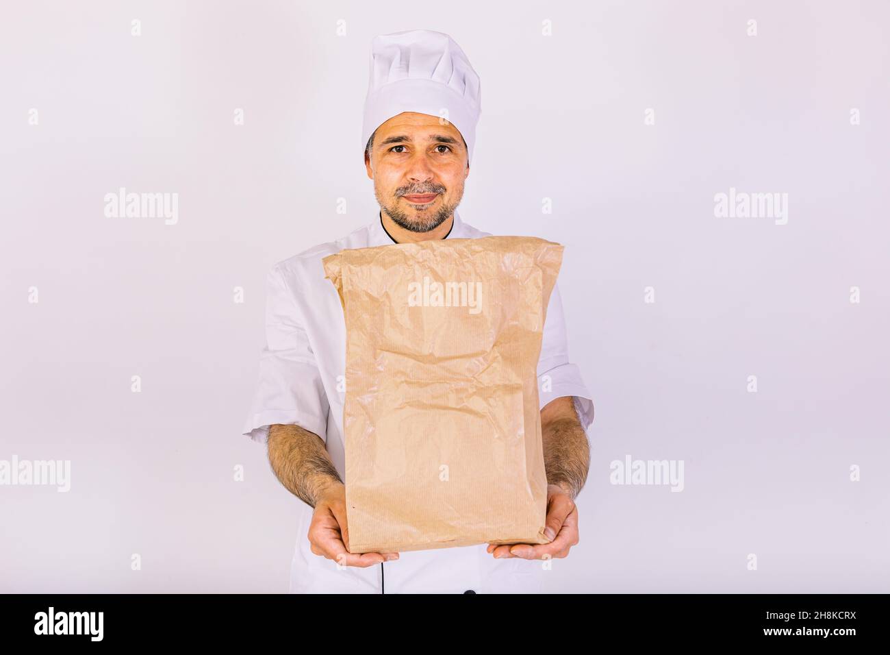 Chef cook wearing white kitchen cap and jacket, holding a paper bag ...