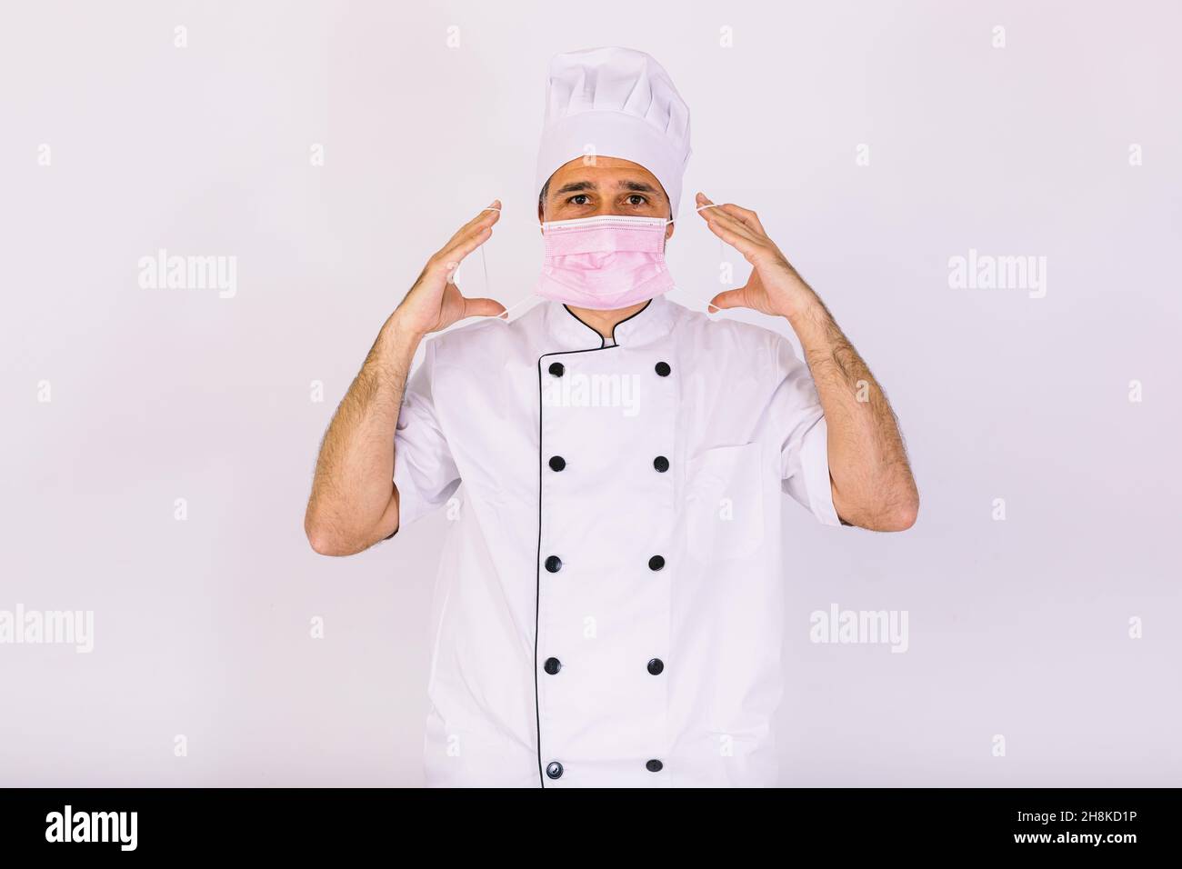 Chef cook wearing kitchen jacket and hat, putting on a pink mask, on ...
