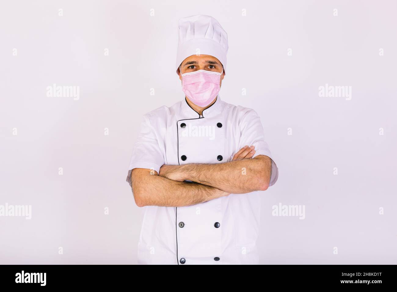 Chef cook wearing kitchen jacket and hat, with pink mask, crossing arms ...